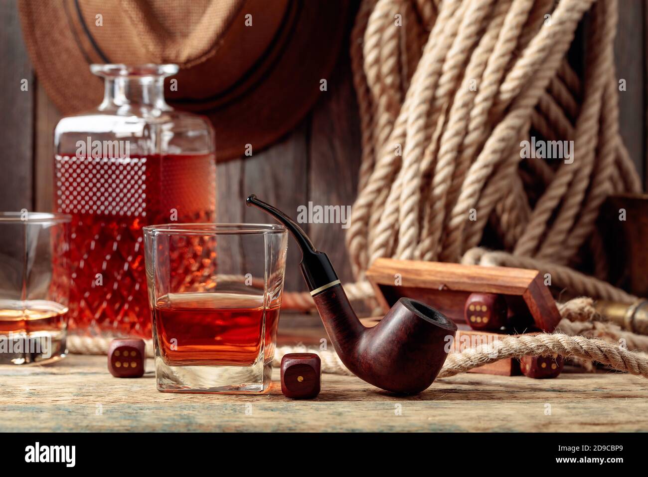 Strong alcoholic drink, pipe, and dice on an old wooden table. In the ...