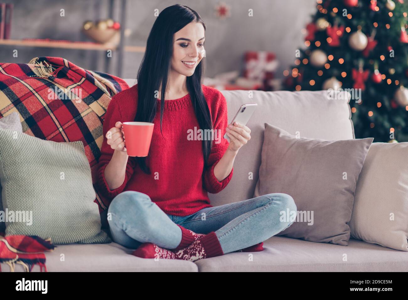 Photo of young pretty girl sit couch hold mug telephone look screen ...