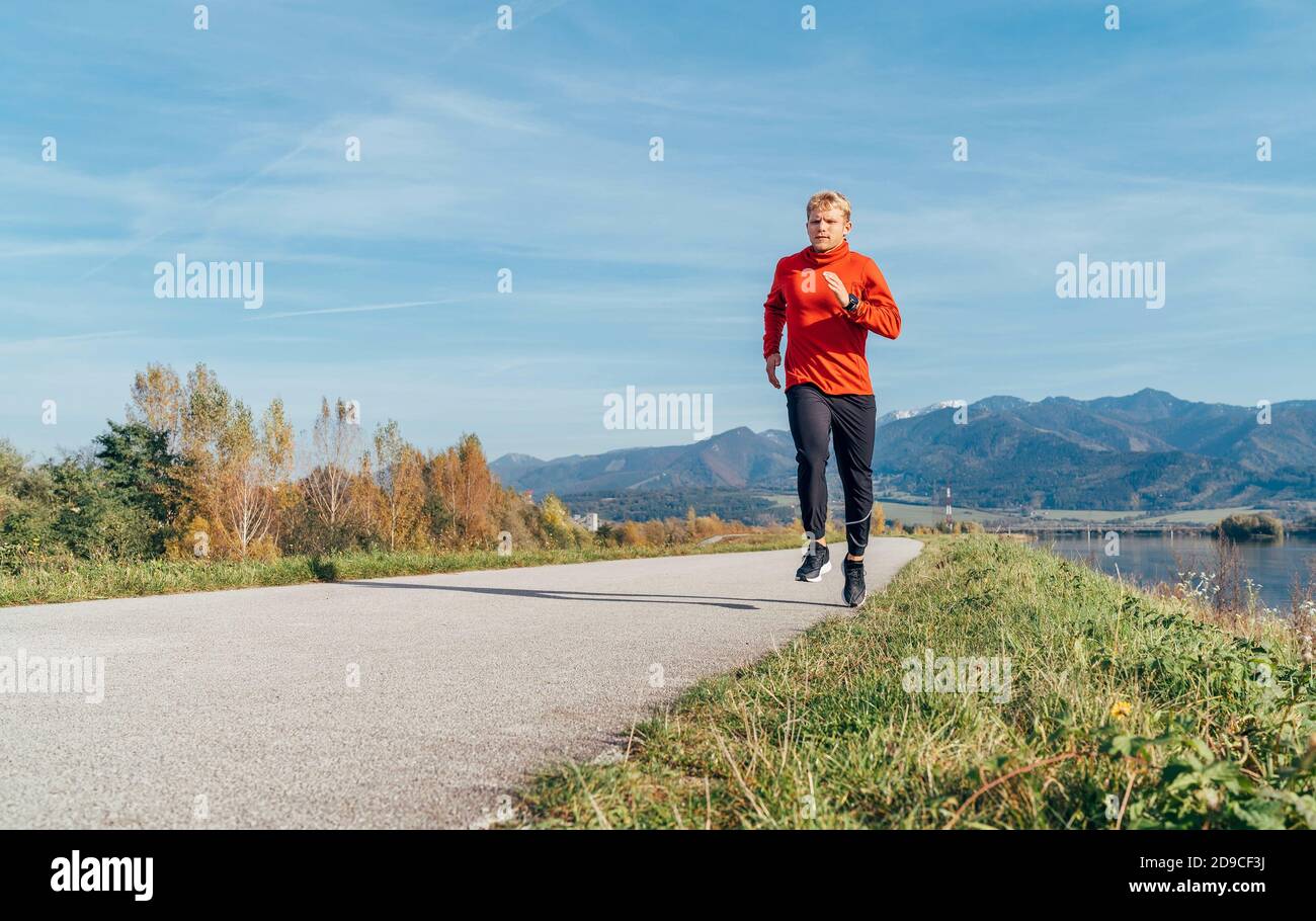 Man dressed in red long sleeve shirt running by the asphalt road with ...
