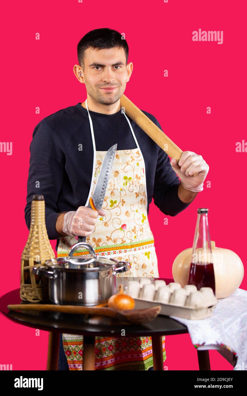 A young man prepares food at home in the kitchen with a knife and ...