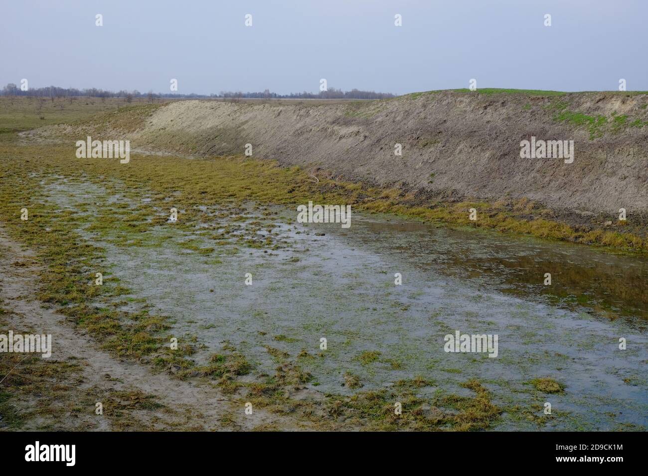 The exposed bottom of a dry pond. A shallow water body. A steep slope ...