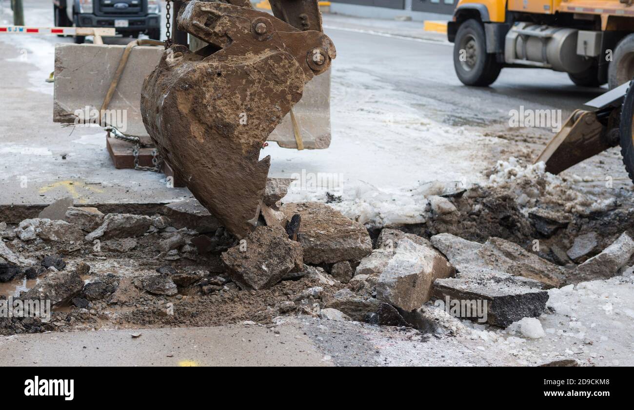 A backhoe removing concrete and asphalt from a frozen sidewalk and road ...