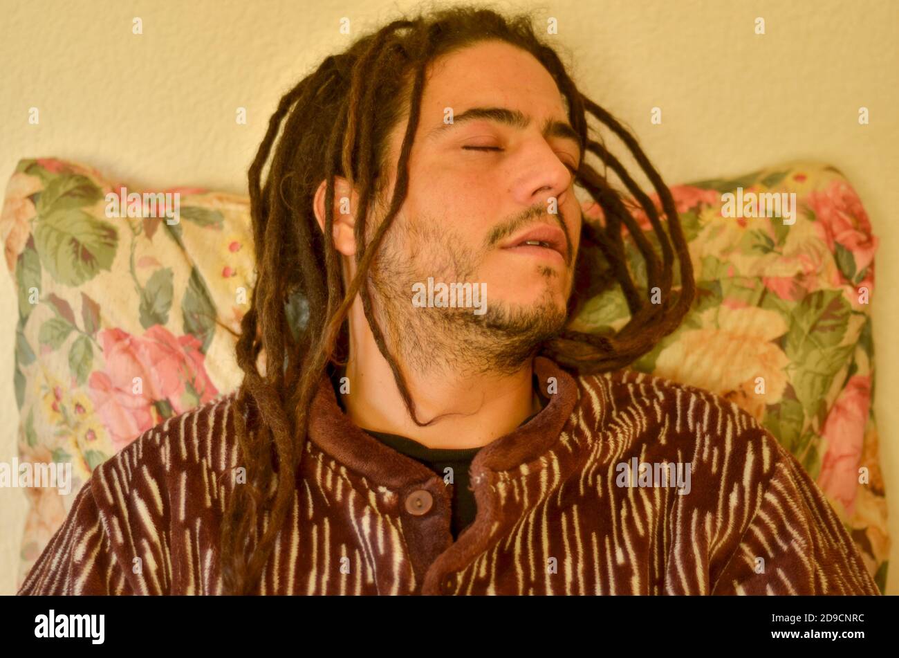 Spanish man with dreadlocks lying with his eyes closed on a colorful ...