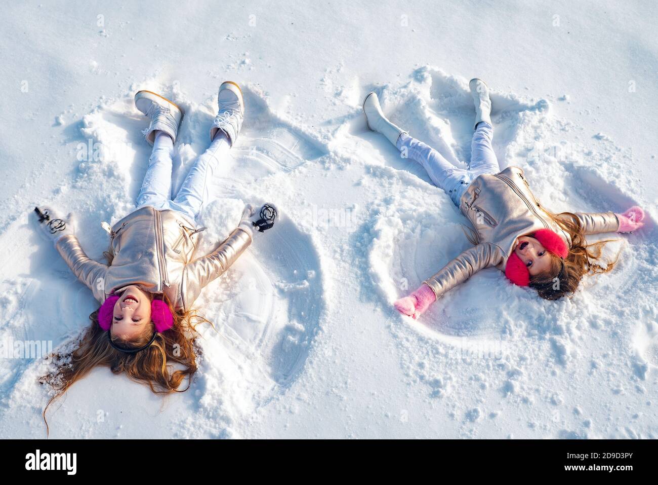 Two little girl making snow angel while lying on snow. Happy girl on a ...