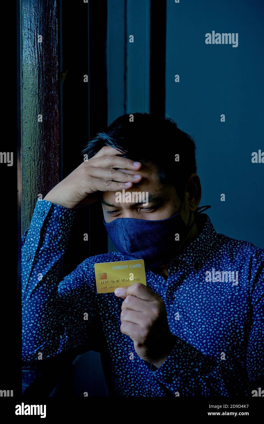 Sad confused and stress man holding credit cards with wearing face mask ...