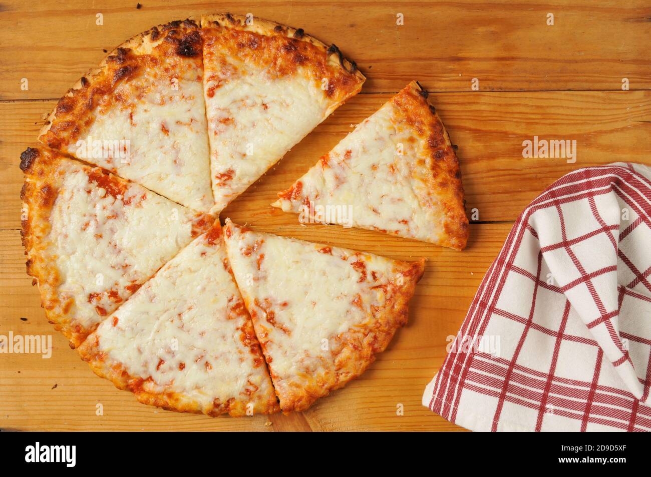 A sliced cheese pizza on a rustic wooden table with a kitchen towel ...