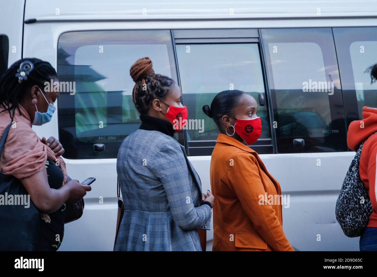 Passengers wearing face masks wait in line to board a public transport ...