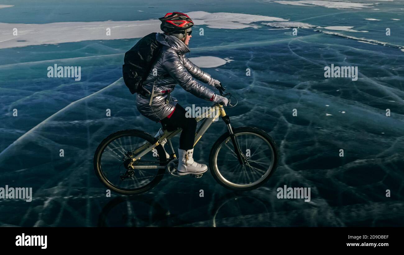 Woman is riding bicycle on the ice. Tires on bike are covered wi Stock ...