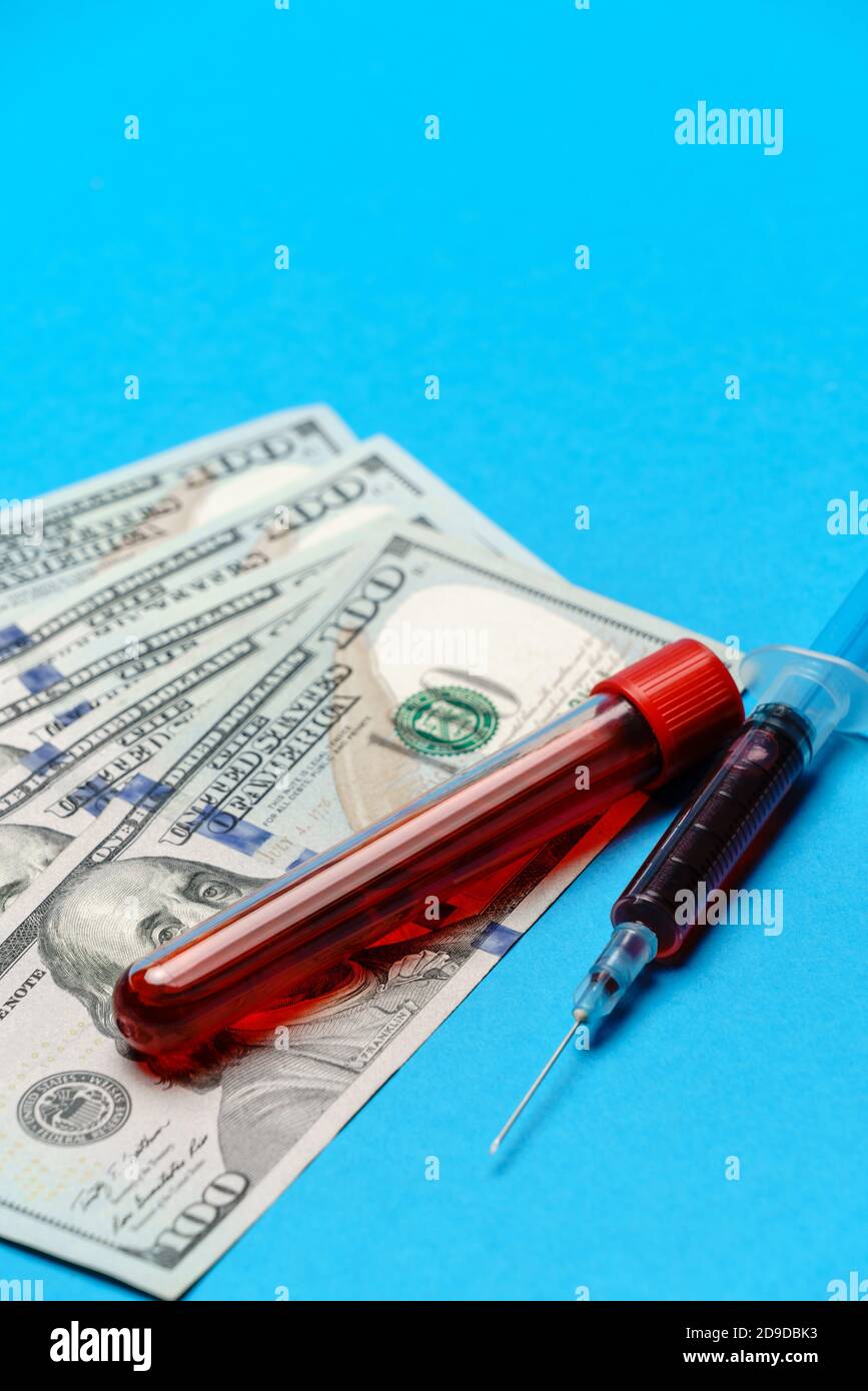 Close up 100 US dollar bills and blood sample in test tube over blue ...