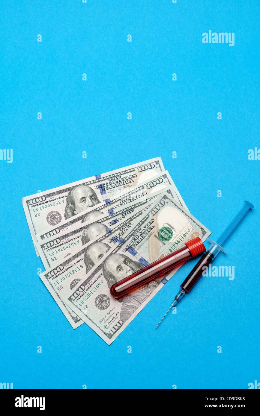 Close up 100 US dollar bills and blood sample in test tube over blue ...
