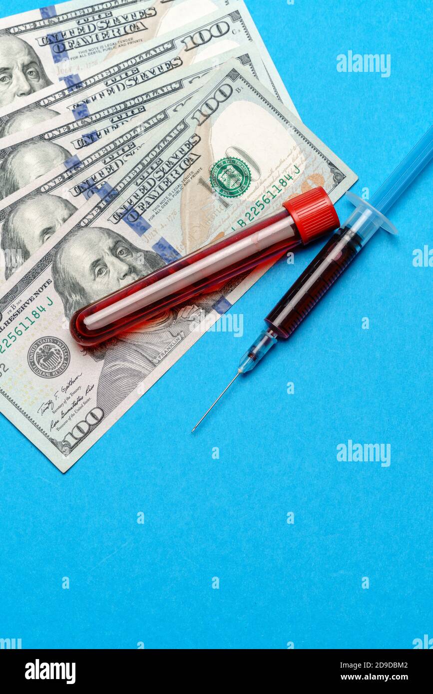 Close up 100 US dollar bills and blood sample in test tube over blue ...