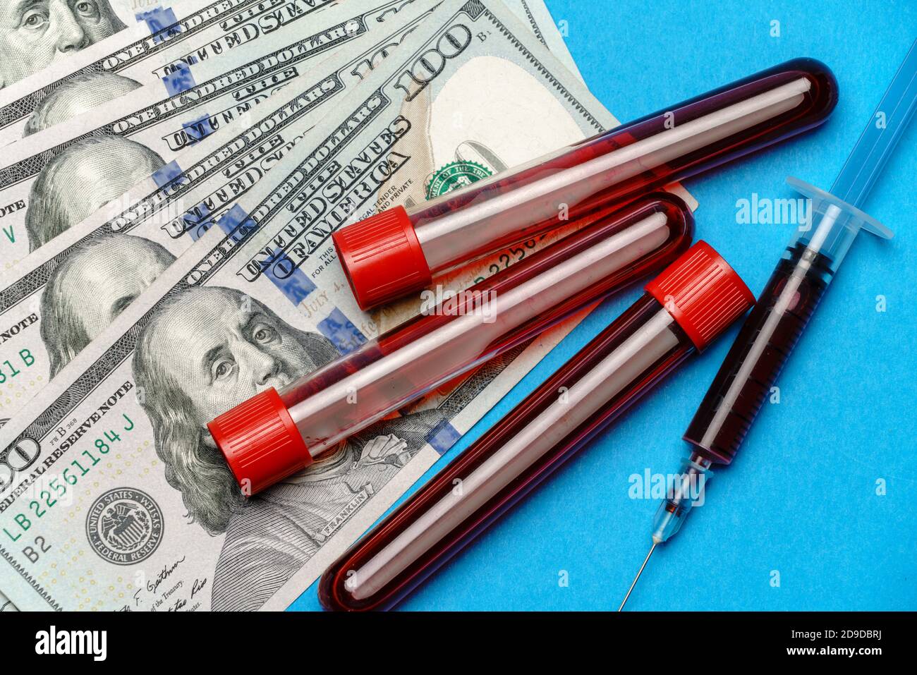 Close up 100 US dollar bills and blood sample in test tube over blue ...