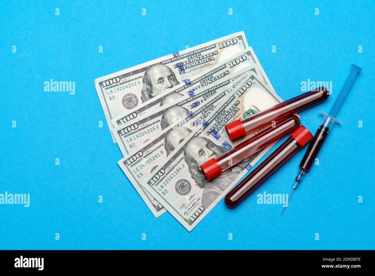 Close up 100 US dollar bills and blood sample in test tube over blue ...