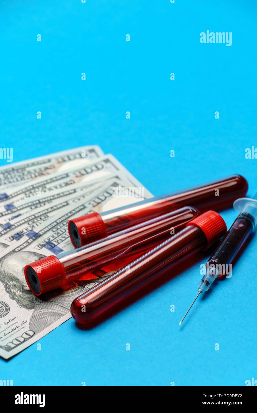 Close up 100 US dollar bills and blood sample in test tube over blue ...