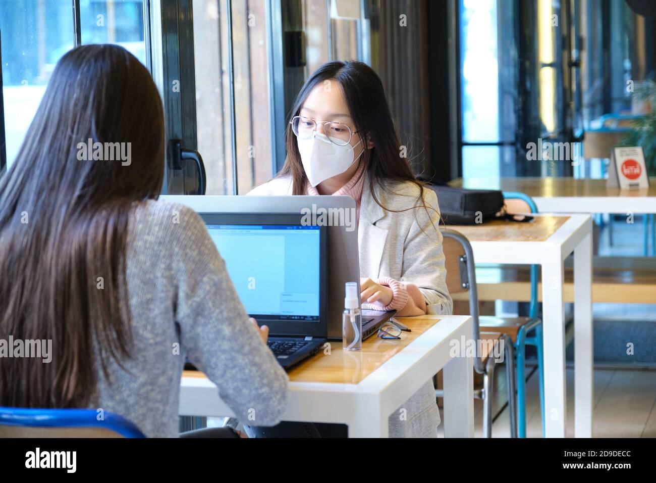 Two female students wearing face masks working on their computers in a ...