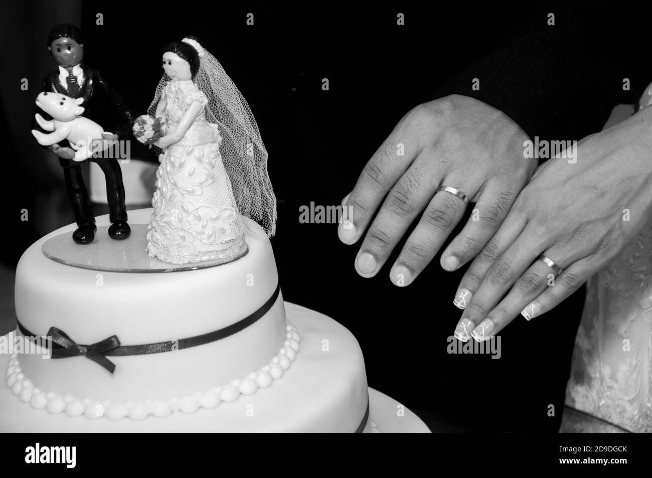 Grayscale shot of hands of a wedding couple over a wedding cake with ...