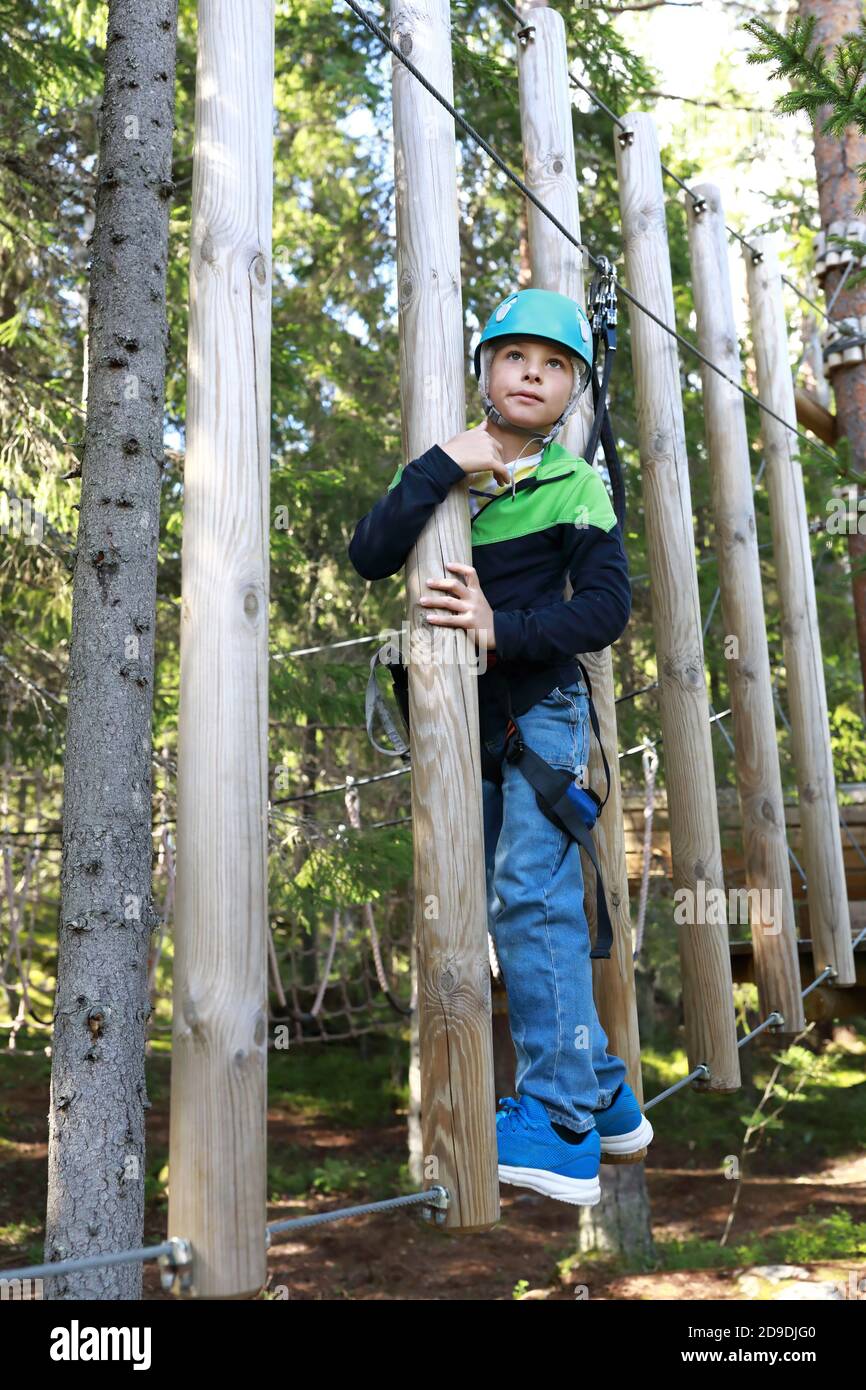 Boy overcoming hanging logs obstacle in forest adventure park, Karelia ...
