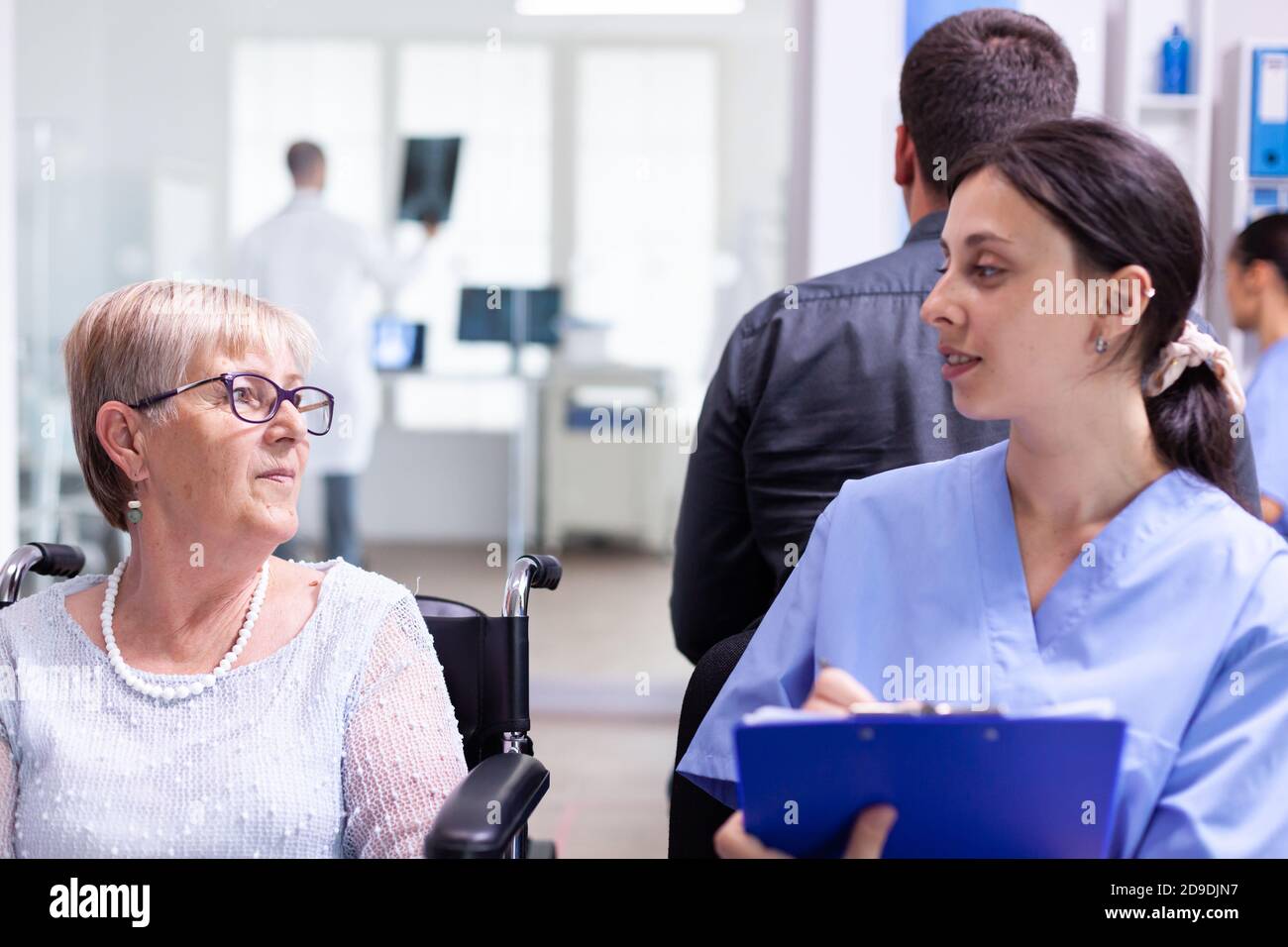 Nurse filing documents while talking with disabled senior woman in ...