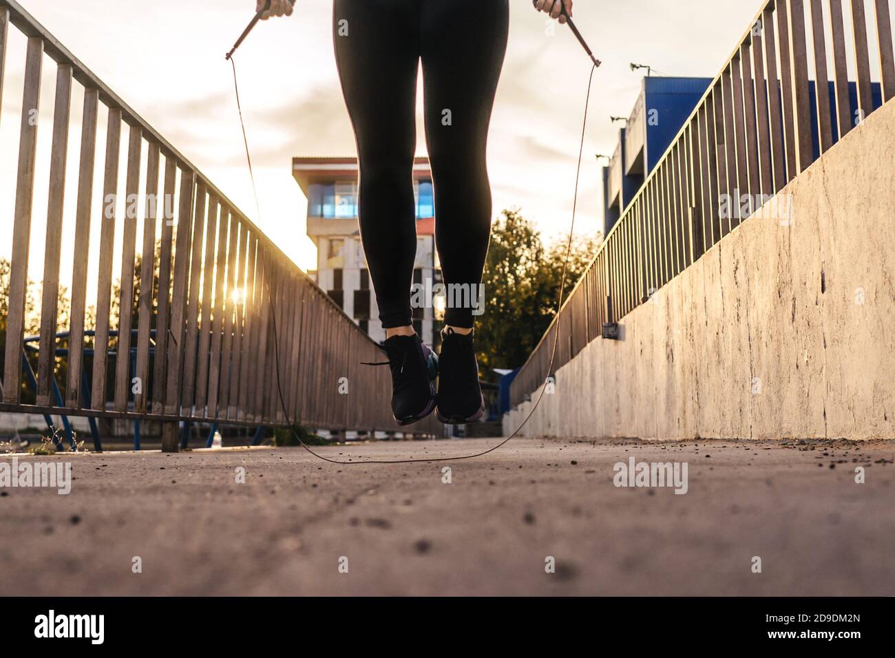 Active young woman jumping with skipping rope outdoors. Sunset light on ...