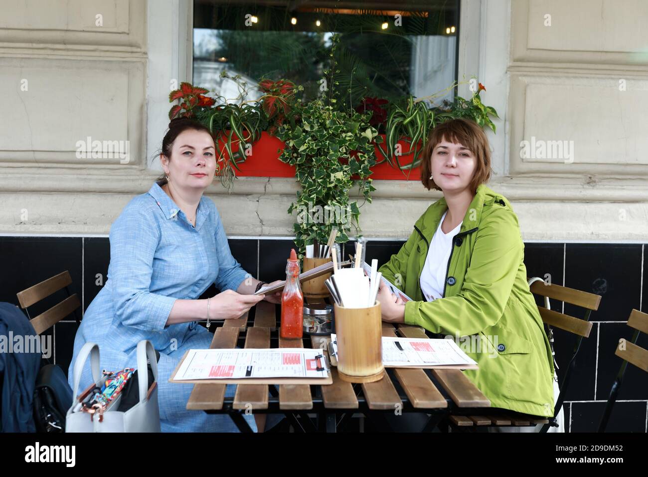 Two women with menu books on veranda of restaurant Stock Photo - Alamy