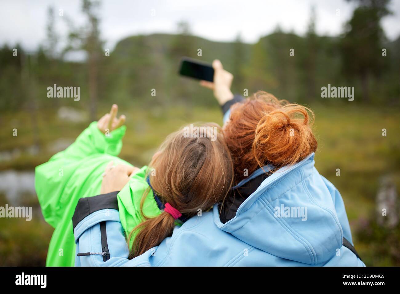Portrait from behind two people holding phone to take selfie in nature ...