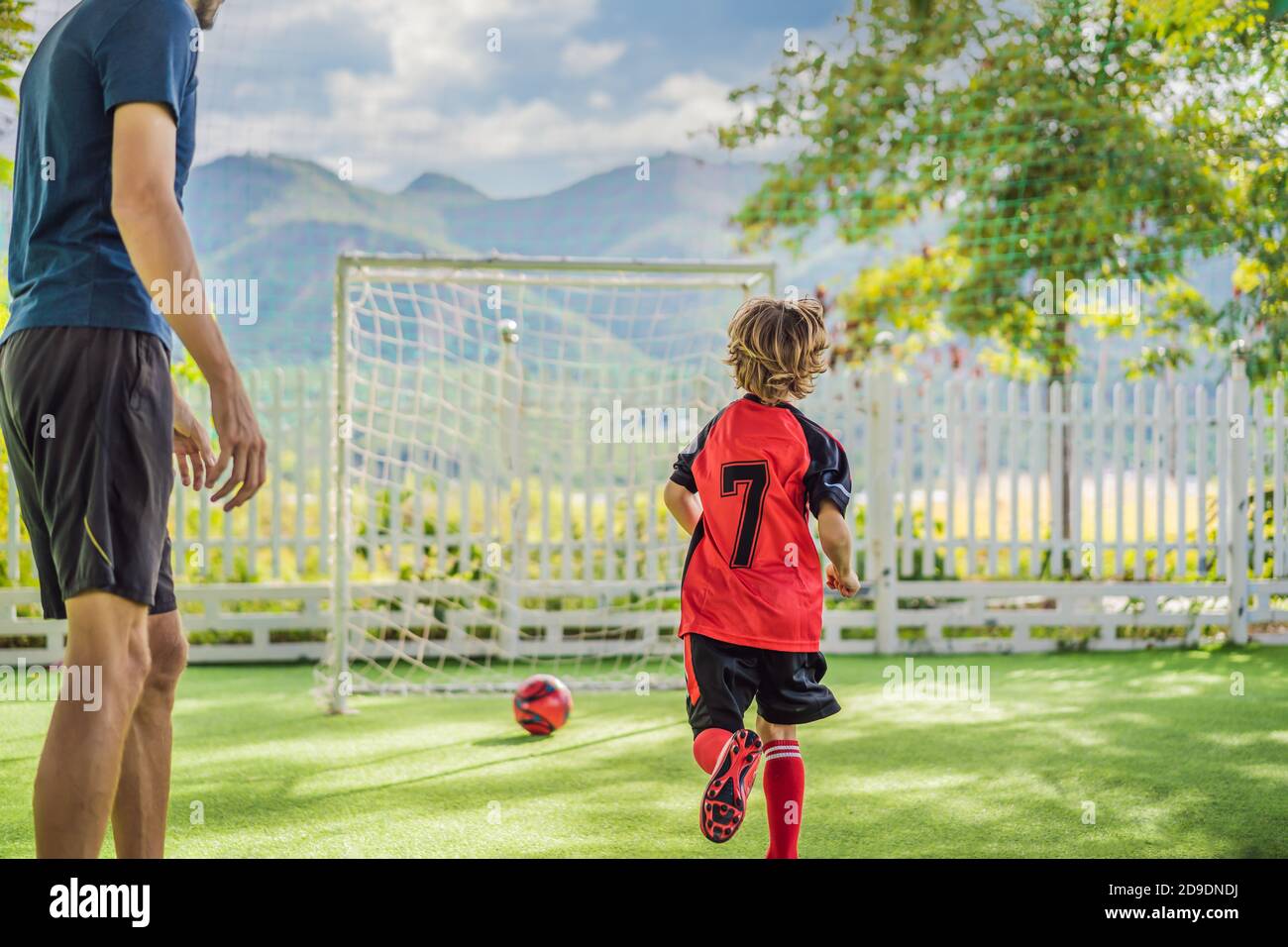 Little cute kid boy in red football uniform and his trainer or father ...