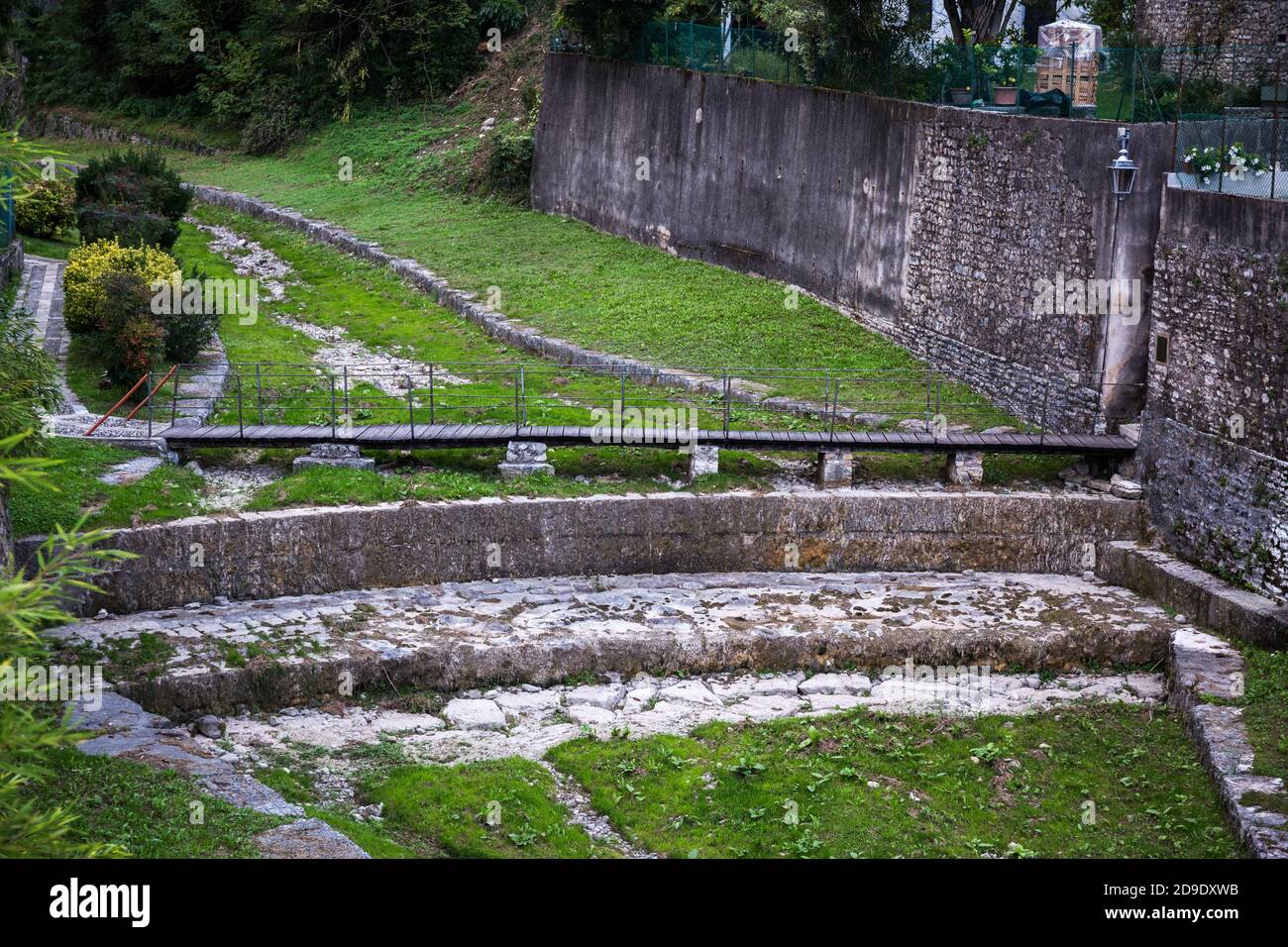 Small wooden bridge next to a stone wall above an empty river without ...