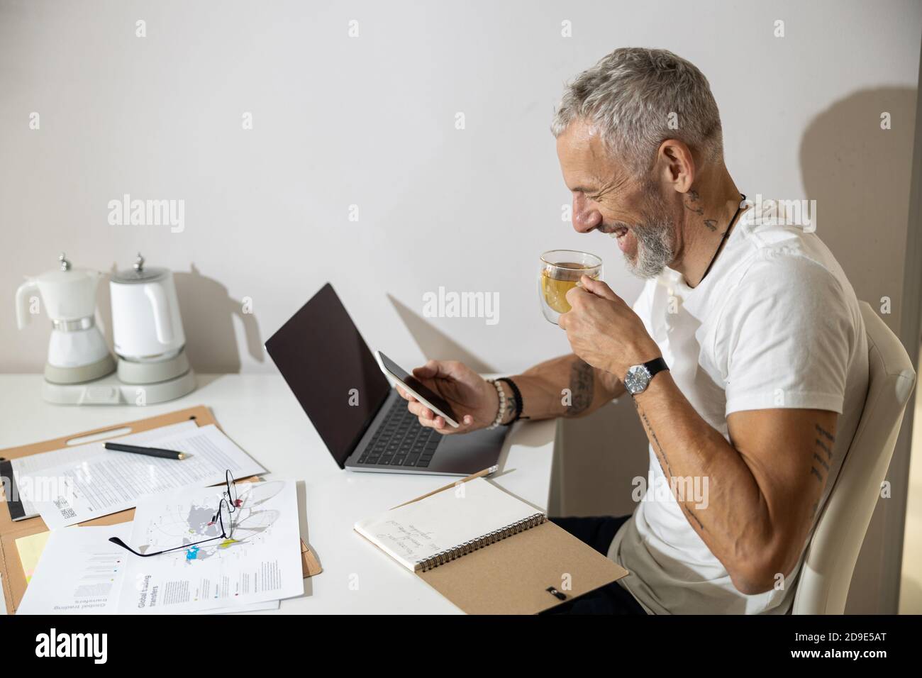 Laughing man finishing his call while drinking tea Stock Photo - Alamy