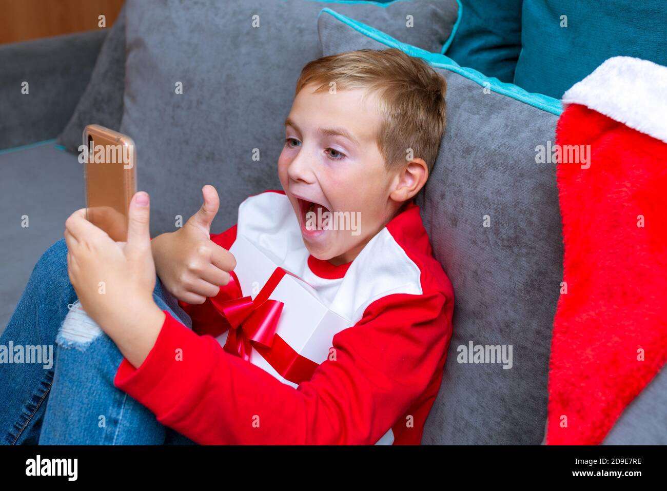 Surprised Handsome kid boy in Santa Claus hat looks at smartphone ...