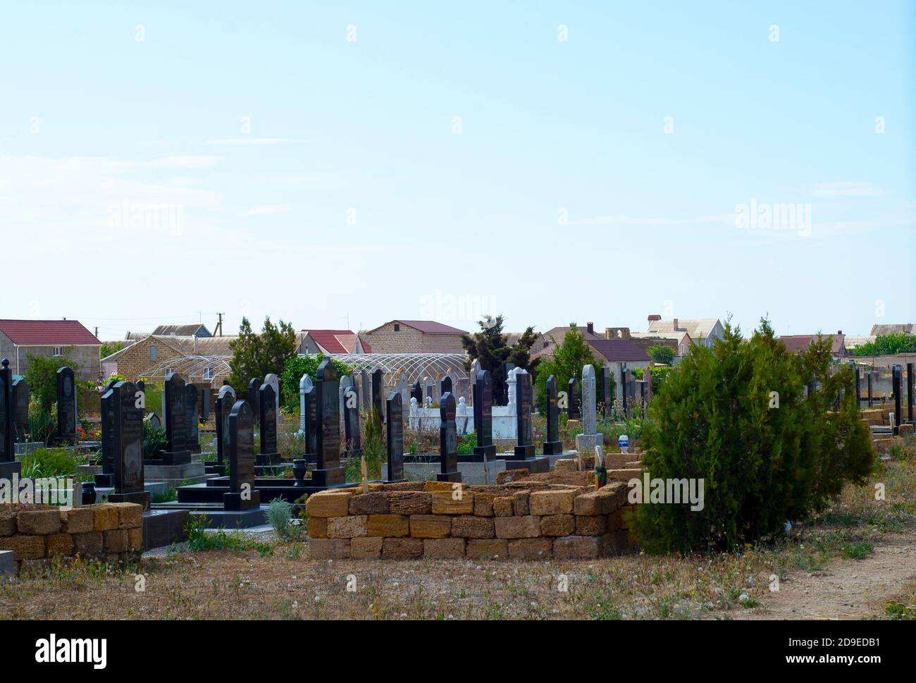 Cemetery on the background of rural houses. Blue sky. Sunny weather ...