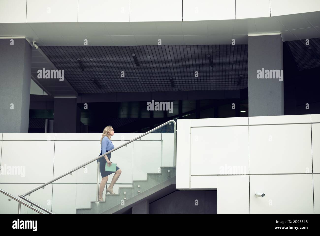 Blonde woman walks the stairs of a public building with a digital ...