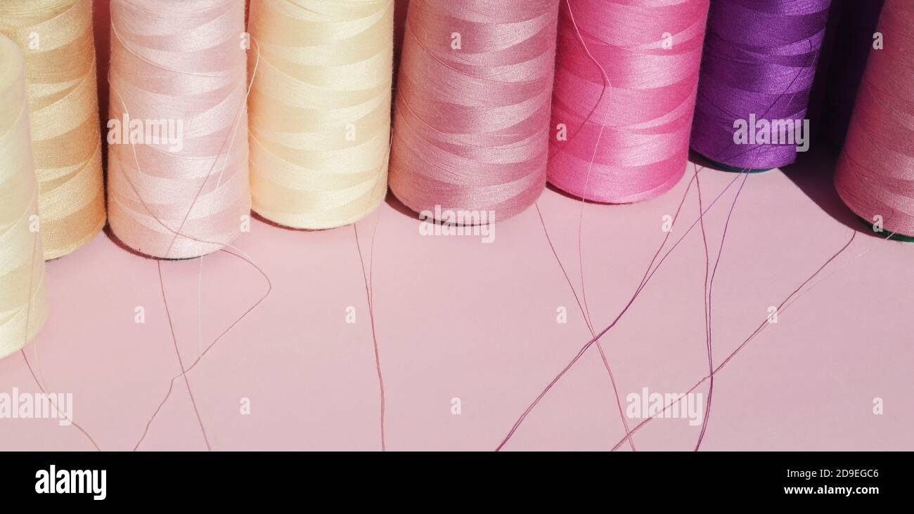 Multi-colored spools of sewing thread on a pink background. Copy space ...