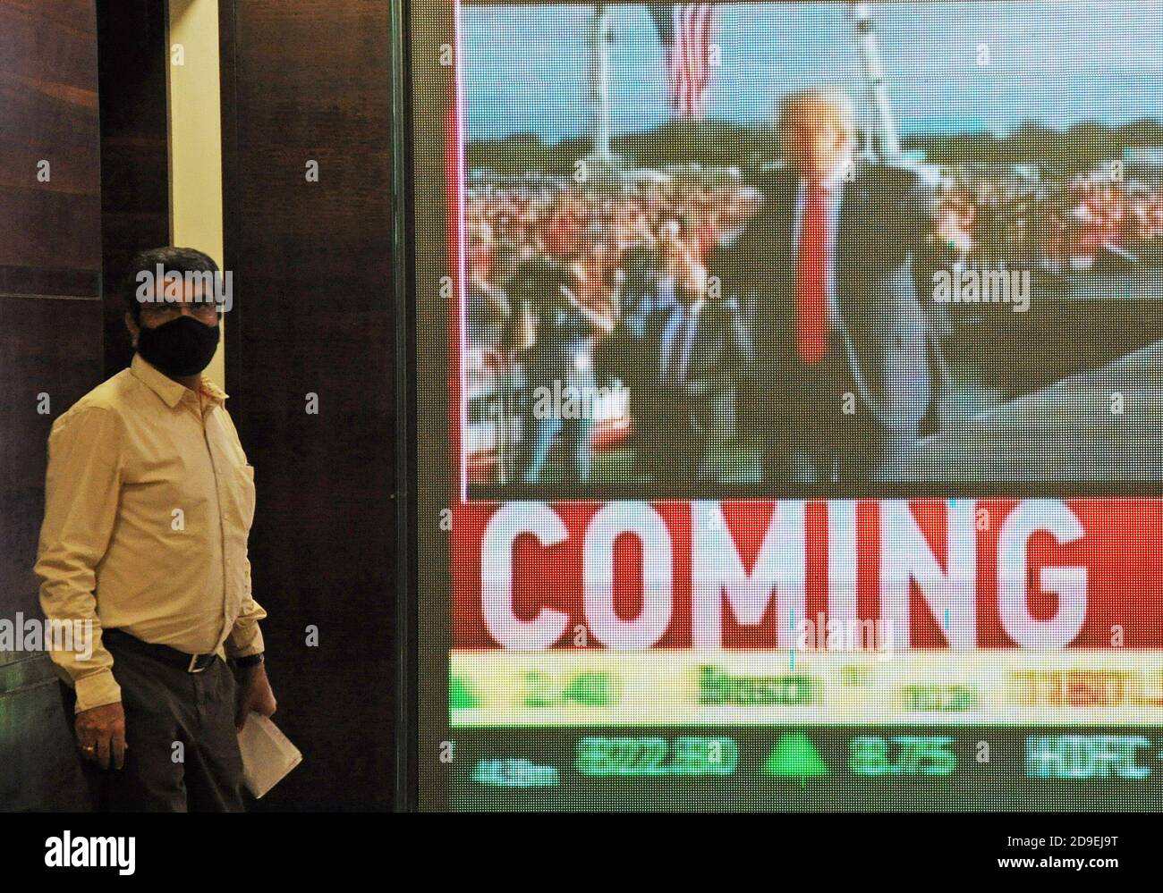 A man wearing a face mask walks past a TV screen displaying the U.S ...