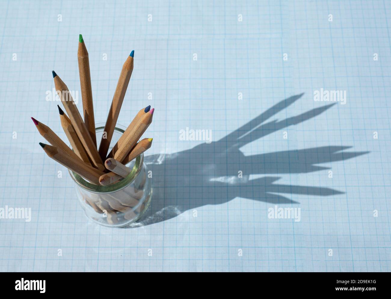 Colored wooden pencils in a glass beaker on a blue background. A shadow ...