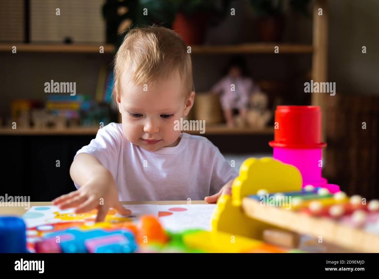 Cute little girl playing alone with many colorful plastic toys at home ...