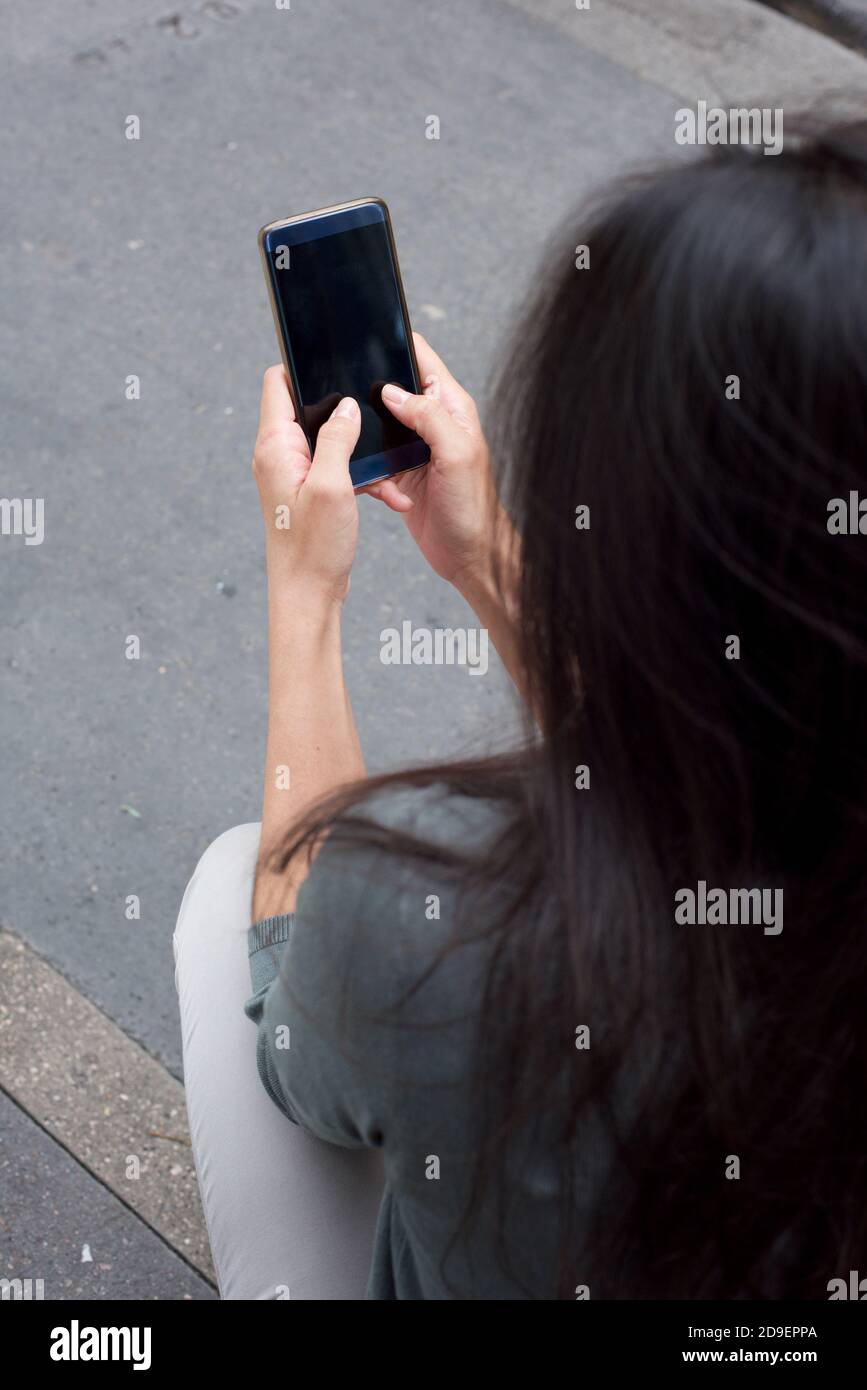 Portrait from behind woman sitting outside looking at mobile phone ...