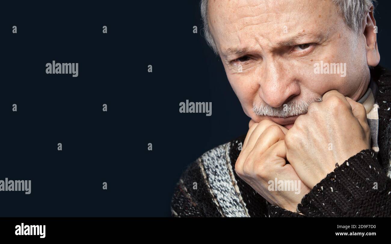 Portrait of senior man prop up the head with his fists on dark blue ...