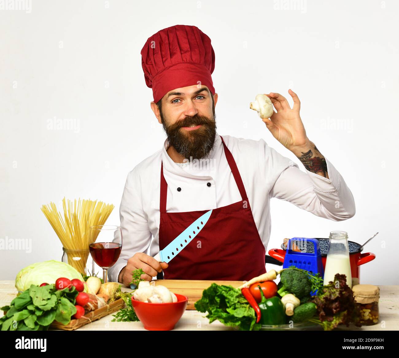 Cook with smile in burgundy uniform sits by kitchen table with ...