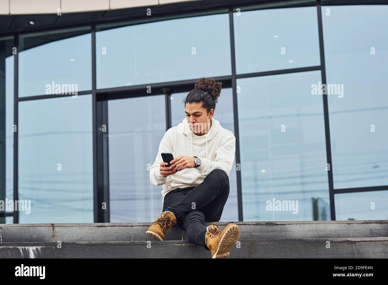 Handsome young man with curly black hair and with smartphone in hands ...