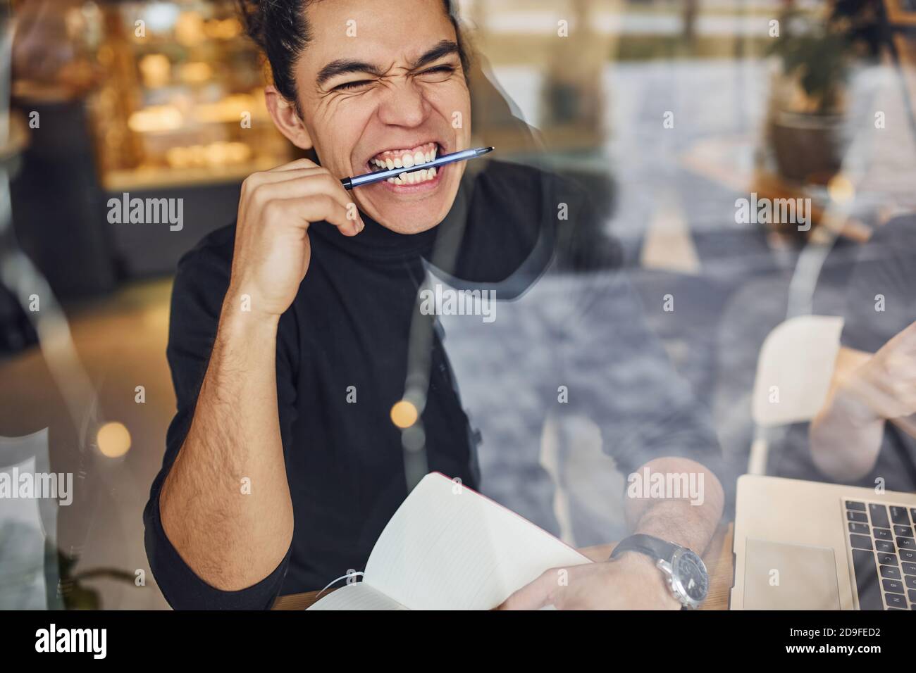 Young male writer with black curly hair sitting indoors in cafe with ...