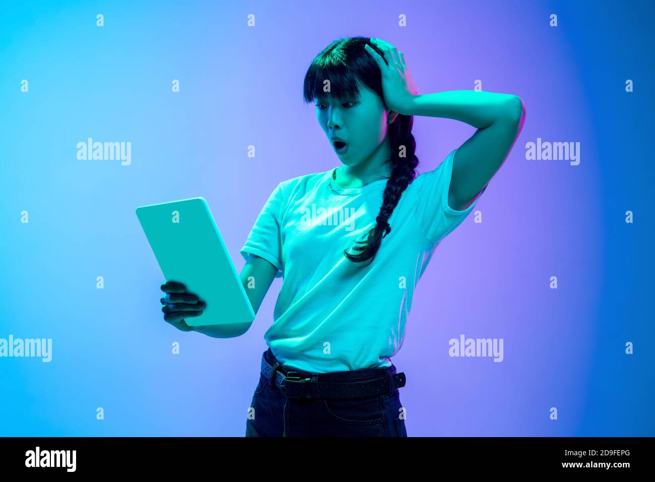 Shocked scrolling tablet. Young asian woman's portrait on gradient blue ...