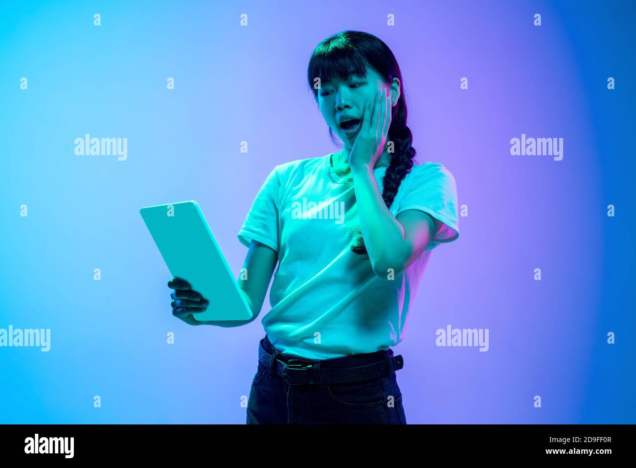 Shocked scrolling tablet. Young asian woman's portrait on gradient blue ...