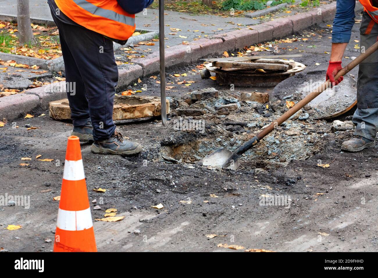 Road workers, dressed in reflective clothing, use a crowbar and a ...