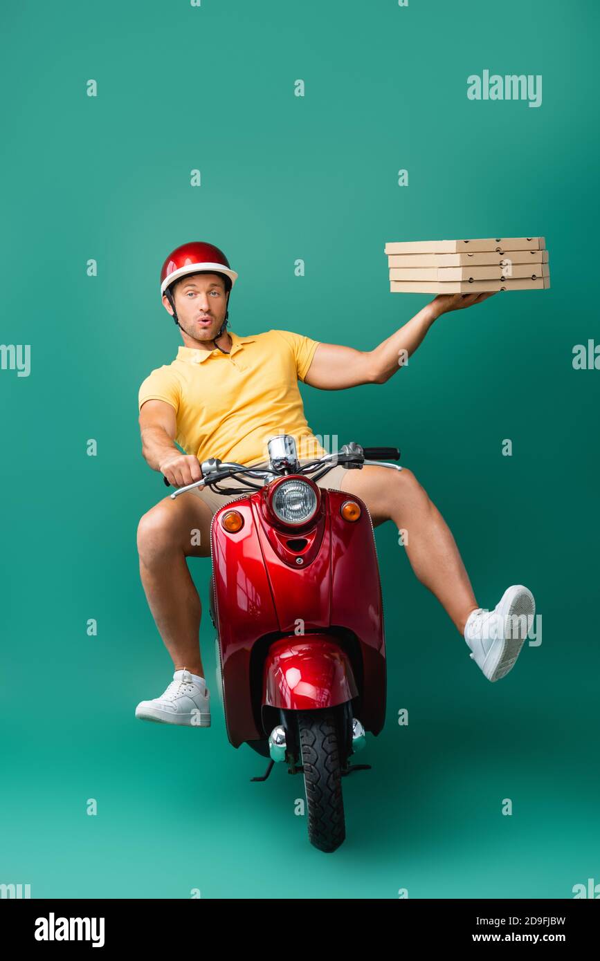 surprised delivery man in red helmet riding scooter while holding pizza ...