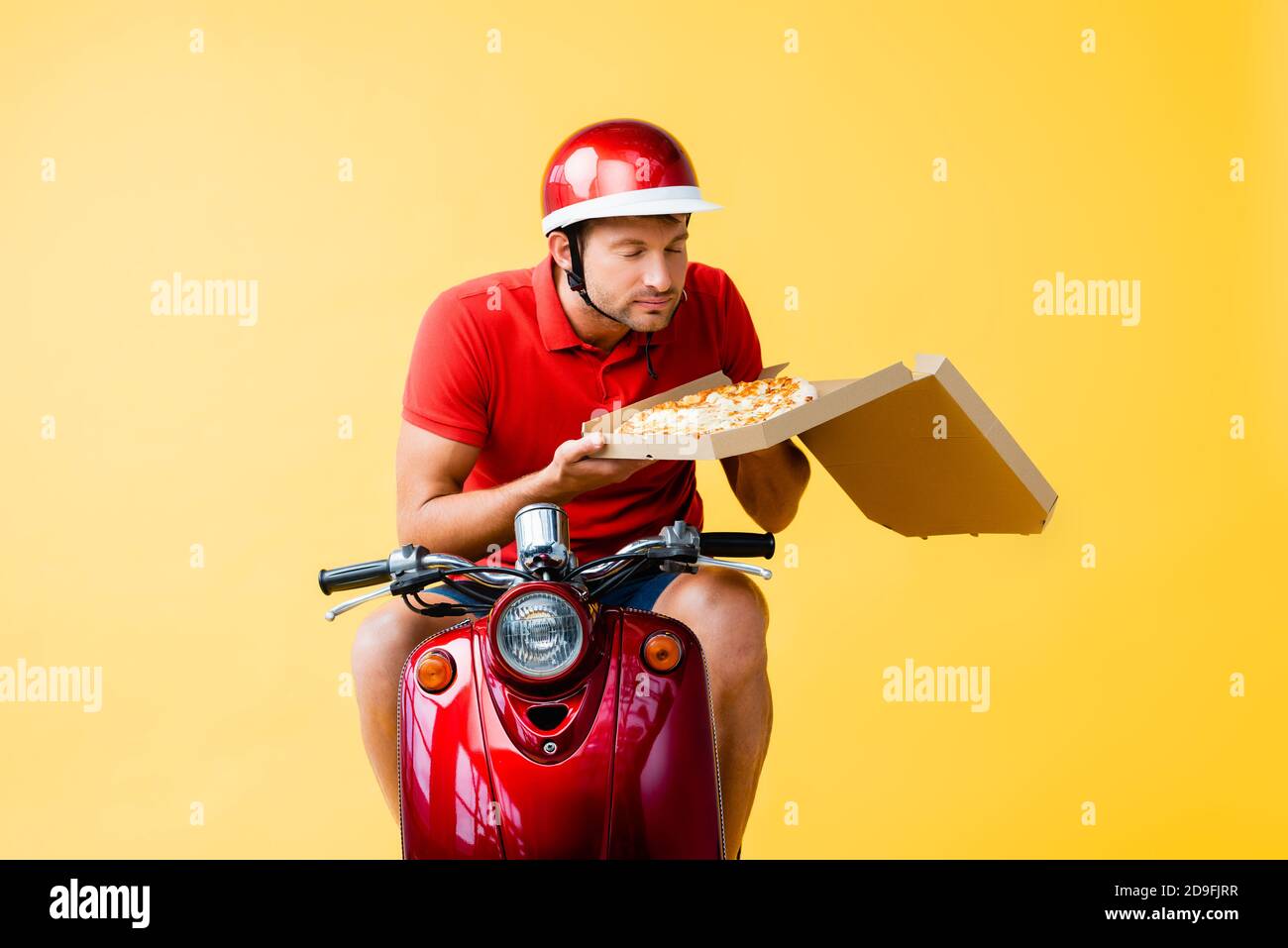 delivery man in helmet riding red scooter and smelling pizza in box on ...