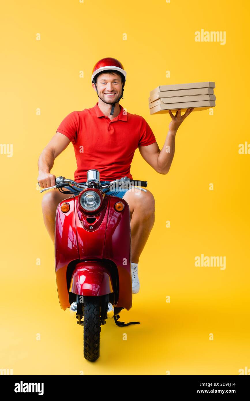happy delivery man in helmet riding scooter and holding carton pizza ...