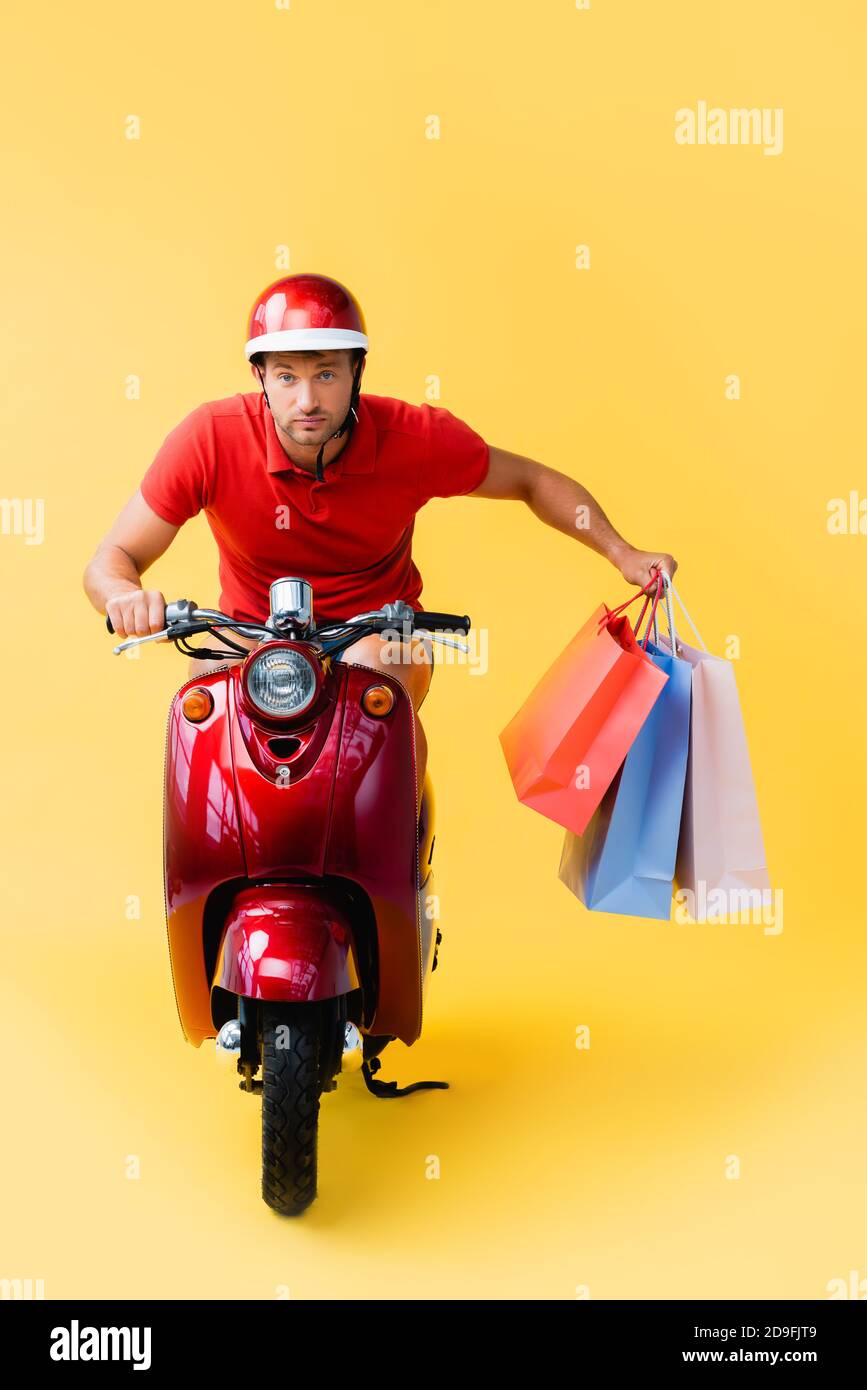 delivery man in helmet riding scooter and carrying shopping bags on ...