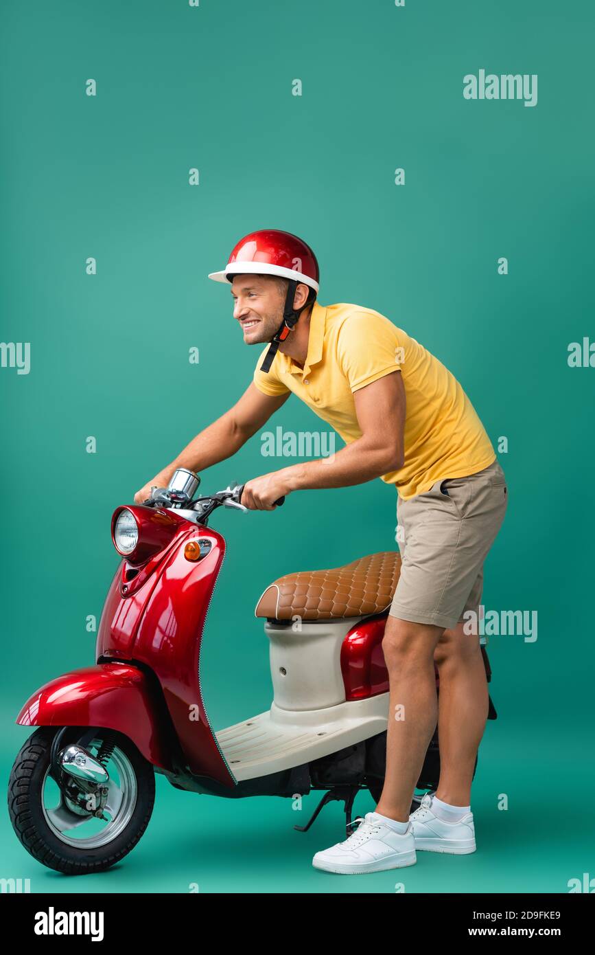 happy delivery man in helmet standing near red scooter on blue Stock ...