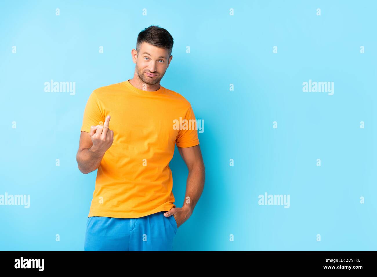 man in t-shirt standing with hand in pocket and showing middle finger ...