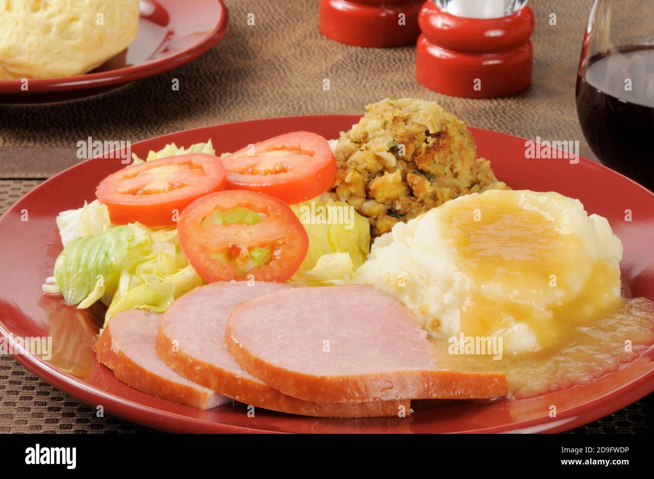 Closeup of a ham dinner with mashed potatoes, gravy, stuffing and a ...